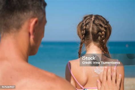 아버지는 해변에서 딸의 등에 보호 크림을 바르고 있습니다 한 남자가 아이의 몸에 자외선 차단제 로션을 들고 있다 바다에 의해 자외선 차단제를 가진 귀여운 어린 소녀 공간을