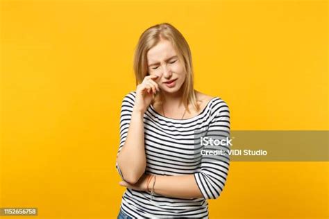 눈을 감고 울고 스튜디오에서 노란 주황색 벽 배경에 고립 된 눈물을 닦아 줄무늬 옷에 불쾌 한 젊은 여자 사람들은 진심으로 감정