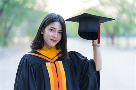 대학원 모자를 들고 학술 가운을 입고 젊은 쾌활한 여성 졸업생의 초상화는 대학 캠퍼스에서 시작 일에 그녀의 대학 학위를 축하합니다 교육에 대한 스톡 사진 및 기타 이미지