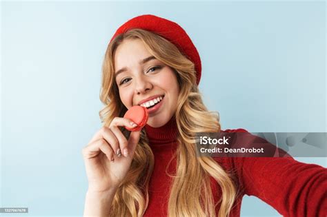 스튜디오에서 파란 배경을 통해 고립 된 셀카 사진을 찍는 동안 마카롱 비스킷을 먹는 빨간 베레모를 입은 매력적인 금발 여성 20 대의 이미지 먹기에 대한 스톡 사진 및 기타