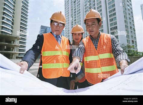 Team Of Vietnamese Engineers Analyzing Construction Blueprint Stock