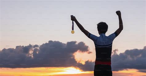 배경에 황금빛 구름으로 장식된 일몰 하늘을 배경으로 금메달을 축하하는 선수의 실루엣 스포츠 경기에서 성공의 정신을 전달하는 데 이상적입니다 사진 Unsplash의