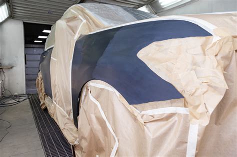 대형 블랙 카는 완전히 종이와 접착 테이프로 덮여 있어 밝은 조명이 있는 차량의 차체 수리를 위한 워크샵에서 사고 후 페인팅 및