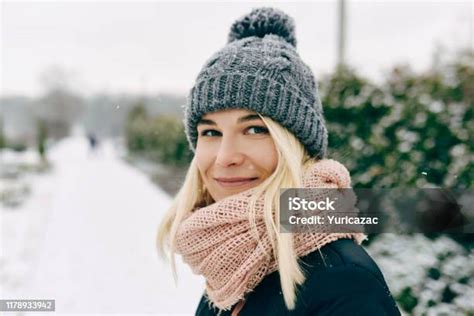 ภาพระยะใกล้ของหญิงสาวสาวสวยผมบลอนด์ยิ้มสวมแจ็คเก็ตฤดูหนาวหมวกถักสีเทาและผ้าพันคอสีชมพ ภาพสต็อก