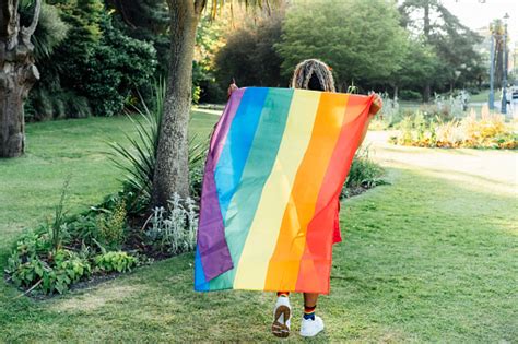 야외에서 무지개 깃발을 들고 있는 뒷모습 여자 젊은 레즈비언 활동가가 사회 운동 Lgbtq의 깃발 상징을 들고 걷고 있다 평등 자유 인권을 위해 싸워라 프라이드의 달을