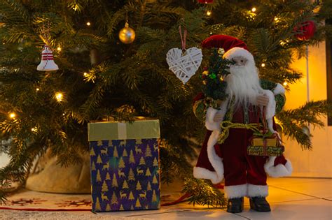 빨간 코트와 모자를 쓴 산타클로스가 선물을 들고 크리스마스 트리 옆에 서 있습니다 12월에 대한 스톡 사진 및 기타 이미지 12월 겨울 계절 Istock