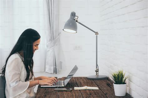 아시아 소녀는 집에 앉아있는 노트북 컴퓨터에서 집에서 일하고 전화를 받고 메모를 작성합니다 사진 Unsplash의 동료 이미지