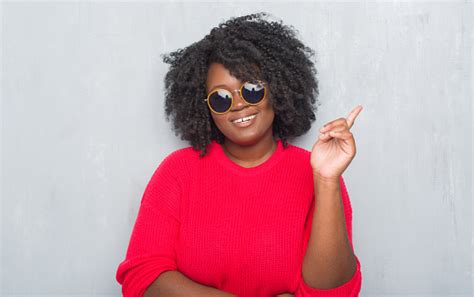 젊은 아프리카계 미국인 플러스 크기 여자 얼굴에 큰 웃음과 함께 복고풍 선글라스를 착용 하는 회색 그런 지 벽 쪽 카메라 보고