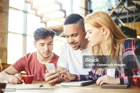 새로운 스마트폰 응용 프로그램을 함께 노력 하 고 책상에 앉아 다양 한 대학생의 그룹 3 명에 대한 스톡 사진 및 기타 이미지