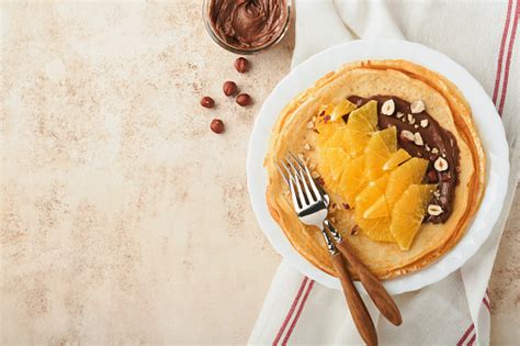 크레페 스게트 와 오렌지 초콜릿 스프레드 헤이즐넛 오렌지 슬라이스 과일을 흰색 접시에 넣고 오래된 콘크리트 소박한 테이블 배경에서 아침 식사를 하는 얇은 크레페 복사 공간을