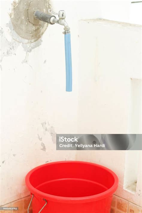 깨끗한 물을 모으기위한 빨간색 플라스틱 양동이와 그 위에는 수도꼭지가 있습니다 타일 벽 배경에 대한 집 구석에 빨간 양동이 복사
