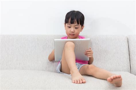 Азиатская китайская маленькая девочка сидя на софе с таблеткой Стоковое Изображение