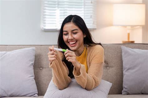 Woman Holding Pregnancy Test With Positive Result Sitting On Couch In Cozy Home Environment