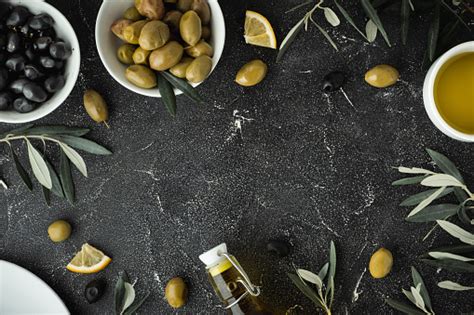 녹색과 검은 색 올리브는 올리브 오일이 든 병 옆에 흰색 그릇에 담겨 있으며 검은 색 배경에 나뭇잎 냉간 압착 오일 한 병 전통적인 그리스와 이탈리아 음식 플랫 레이 복사