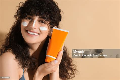 베이지색 배경에 자외선 차단제 튜브를 들고 얼굴에 자외선 차단 크림을 바르고 있는 아름다운 젊은 여성 텍스트를 위한 공간 20 24세에 대한 스톡 사진 및 기타 이미지