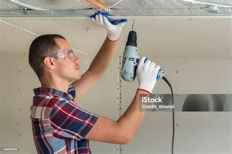 반짝이는 알루미늄 호일로 절연 천장에 전기 드라이버를 사용하여 금속 프레임에 건식 벽체 천장을 고정 고글에 젊은 남자 리노베이션 건설 직접 개념을 수행하십시오 Diy에 대한