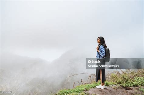 산 꼭대기에서 휴식을 취하고 안개 낀 계곡의 전망을 즐기는 배낭을 가진 젊은 여성 관광객 여자에 대한 스톡 사진 및 기타 이미지