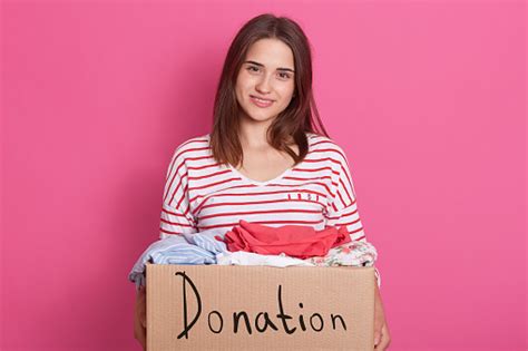 가난한 사람들을 위한 옷이 달린 종이 상자를 들고 자원봉사하는 미소 짓는 소녀의 초상화를 클로즈업하고 기부를 하는 여성 여성은