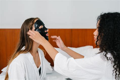 뷰티 스킨 케어 개념 친구 얼굴에 화장용 얼굴 마스크를 적용하는 어린 소녀 보습 시트 마스크에 아름다운 백인 여성 20 29세에