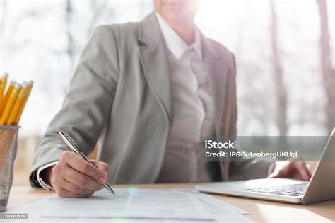 사무실에서 창에 대 한 책상에서 노트북과 함께 앉아있는 동안 종이에 쓰는 성숙한 사업가의 중간 부분 40 44세에 대한 스톡 사진 및 기타 이미지 Istock