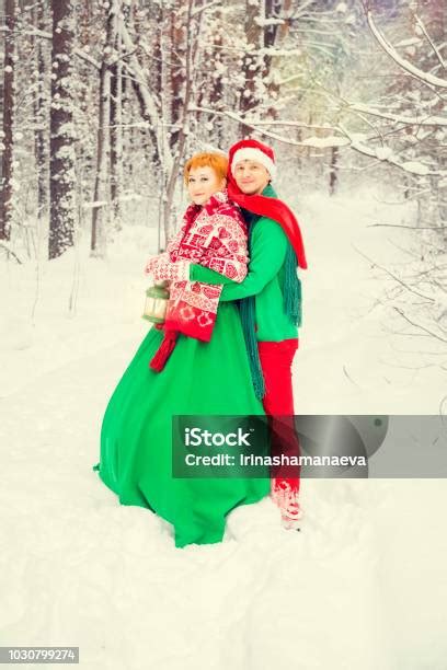 젊은 부부 남자와 여자 남편과 아내는 산타의 도우미 가슴 가득 선물 및 거 대 한 사탕으로 눈 아래 겨울 숲에서의 엘 프의