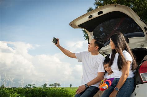 전기 자동차를 타고 풍력 발전 단지에서 시간을 보내는 행복한 가족 풍력 터빈 발전기에서 충전소까지 풍력 터빈 발전기의 깨끗하고 재생 가능한 에너지 3 명에 대한 스톡 사진