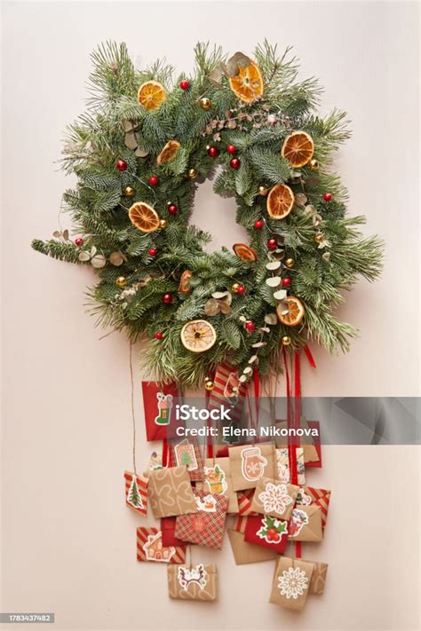 크리스마스 공과 마른 오렌지 조각으로 장식 된 전나무 가지 화환과 새해 강림절 달력이 매달려 있습니다 빨간 리본에 아름 다운 공예 봉투 강림절 달력에 대한 스톡 사진 및