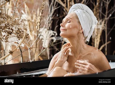 Pleased Middle Aged Woman With Towel On Head And Closed Eyes Taking Bath In Modern Apartment