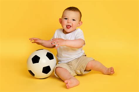 행복한 아기 소년은 노란색 스튜디오 배경에 축구 공을 가지고 놀고 공간을 복사합니다 웃는 아이는 큰 공으로 축구를하는 법을