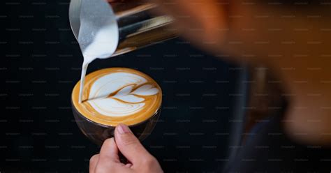 커피 컵에 에스프레소 커피에 우유 거품을 붓는 남자 바리스타의 손을 클로즈업하여 커피 라떼 아트를 고객에게 제공합니다 중소 기업 카페 및 식당 주인 및 아르바이트 작업