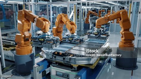 고급 주황색 산업용 로봇 팔은 자동화된 생산 라인에서 Ev 배터리 팩을 조립합니다 자동차 공장 내부의 로봇 팔 줄은 배터리를 조립합니다 현대 전기 자동차 스마트 공장 제조에
