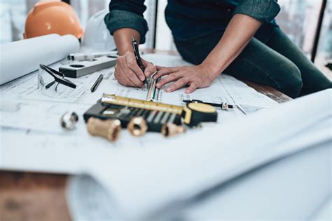 사무실 책상과 계산기 삼각형 눈금자 안전 안경 나침반 블루프린트의 버니어 캘리퍼에서 도면 검사 및 쓰기로 작업하는 엔지니어링 엔지니어 건축가 산업 및 공장 개념 개발에 대한