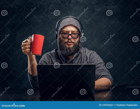 A Hacker Sits Behind A Laptop Holding A Cup Of Coffee And Working With Programs In A Dark Room