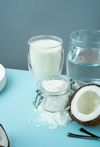 코코넛 제품 고기가 반으로 자른 오픈 코코넛 유리 항아리에 코코넛 파우더 푸른 배경에 우유를 심는 다 등등 투영 공간을 복사합니다 개념 대체 우유 식물성 가루로 빻은에 대한