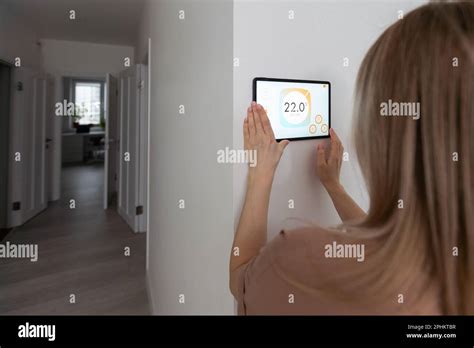 Woman Controlling Home With A Digital Touch Screen Panel Installed On The Wall In The Living