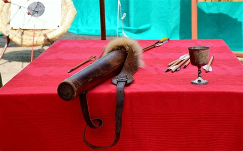 양궁 대회 기간 동안 폴란드 시골에서 화창한 날에 는 황동 컵 다양한 화살표와 볼트 그리고 에크루 토끼 모피로 완성 된 떨림이 있는 빨간 천으로 덮인 테이블이 배치됩니다 0