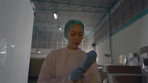 여성 영양사 또는 관리자 생산 라인 또는 헤어넷 및 멸균 의류 및 장갑을 착용 한 감독자는 노란색 플라스틱 먼지 커튼을 통과하여 Gmp 표준에 따라 소비자 제품 생산