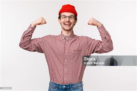 빨간 비니와 안경 플렉스 팔뚝에 격려하고 활기찬 젊은 자신감 슬림 남자의 허리 업 초상화 그의 근육이 강하고 강력한 것을 보여주는 서 흰색 배경 근육질 체격에 대한 스톡