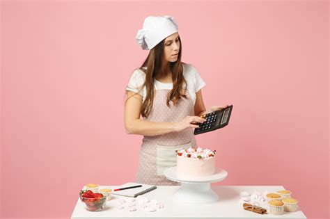 요리사 요리 과자 또는 베이커 앞치마 흰색 티셔츠 모자 요리사 모자 요리 케이크 또는 테이블 홀드 계산기에 분홍색 파스텔 배경에