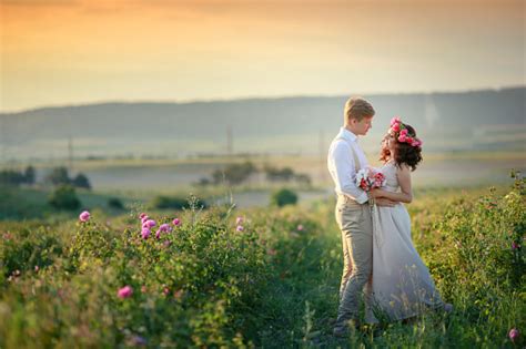 행복 한 젊은 부부 남자와 여자 성인 로맨틱 한 가족입니다 밀 밭에서 석양을만 나 보세요 행복 한 미소 그녀의 손에 있는 소녀는 장미에서 선물 꽃의 꽃다발을 보유 하 고