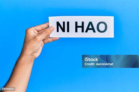 고립 된 파란색 배경 위에 중국어 인사 니 하오 단어 종이를 들고 히스패닉 남자의 손 경례에 대한 스톡 사진 및 기타 이미지