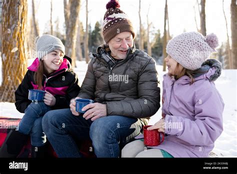 Happy Grandpa And Granddaughters Enjoying Hot Cocoa In Winter Woods