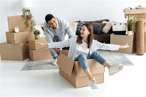 새 집 이전 행복한 혼혈 젊은 가족 커플 백인 소녀와 라틴계 남자는 골판지 상자를 가지고 놀고 있고 여자는 안에 앉아 남자가