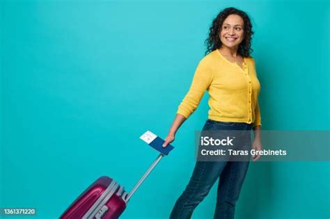 행복한 곱슬 머리 여자 밝은 노란색 스웨터와 탑승권과 항공권 여권을 들고 파란색 청바지를 입은 여행자 미소 복사 공간과 파란색