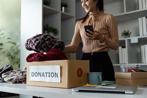 스마트폰과 사무용품이 있는 집에서 골판지 상자에 기부를 위해 옷을 정리하는 여성 Brand Name Smart Phone에 대한 스톡 사진 및 기타 이미지 Brand