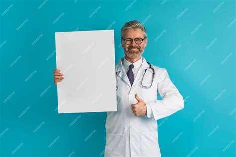 Beau Médecin Mature Montrant Une Pancarte Vierge Et Le Pouce Vers Le