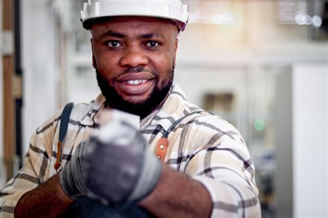 중년의 아프리카 목수의 초상화는 하얀 헬멧을 쓰고 나무 판자를 측정하고 조준하고 노동자는 목공 작업장에서 목재 가구를 만들고 목공 작업장에서 장인이 일한다 40 44세에