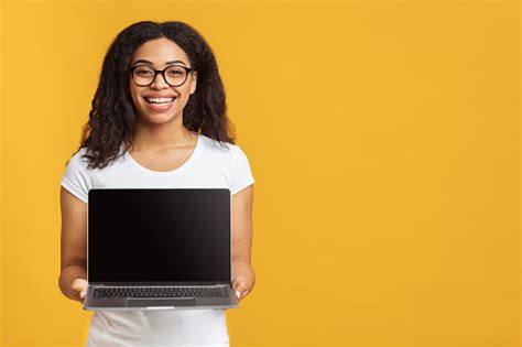 노란색 스튜디오 배경 빈 공간을 통해 카메라에 노트북 빈 화면을 보여주는 행복한 아프리카 계 미국인 여성 노트북에 대한 스톡 사진 및 기타 이미지 Istock