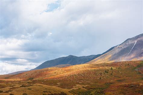 햇볕이 잘 드는 언덕과 극적인 흐린 하늘 아래 산맥 실루엣이있는 잡다한 가을 풍경 산에서 생생한 가을 색상 다색 언덕의 햇빛과 변화하는 날씨의 비오는 구름 0명에 대한 스톡