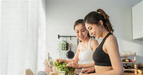 아시아의 젊은 두 여성 형제는 부엌에서 샐러드를 요리하는 운동복을 입고 있다 활동적인 아름다운 소녀 여동생은 행복을 느끼고 야채 건강 식품을 먹고 다이어트를 즐기고 집에서